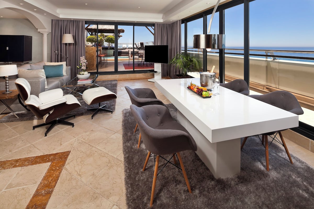 Quarto de hotel moderno com uma varanda espaçosa, área de refeições e televisão.