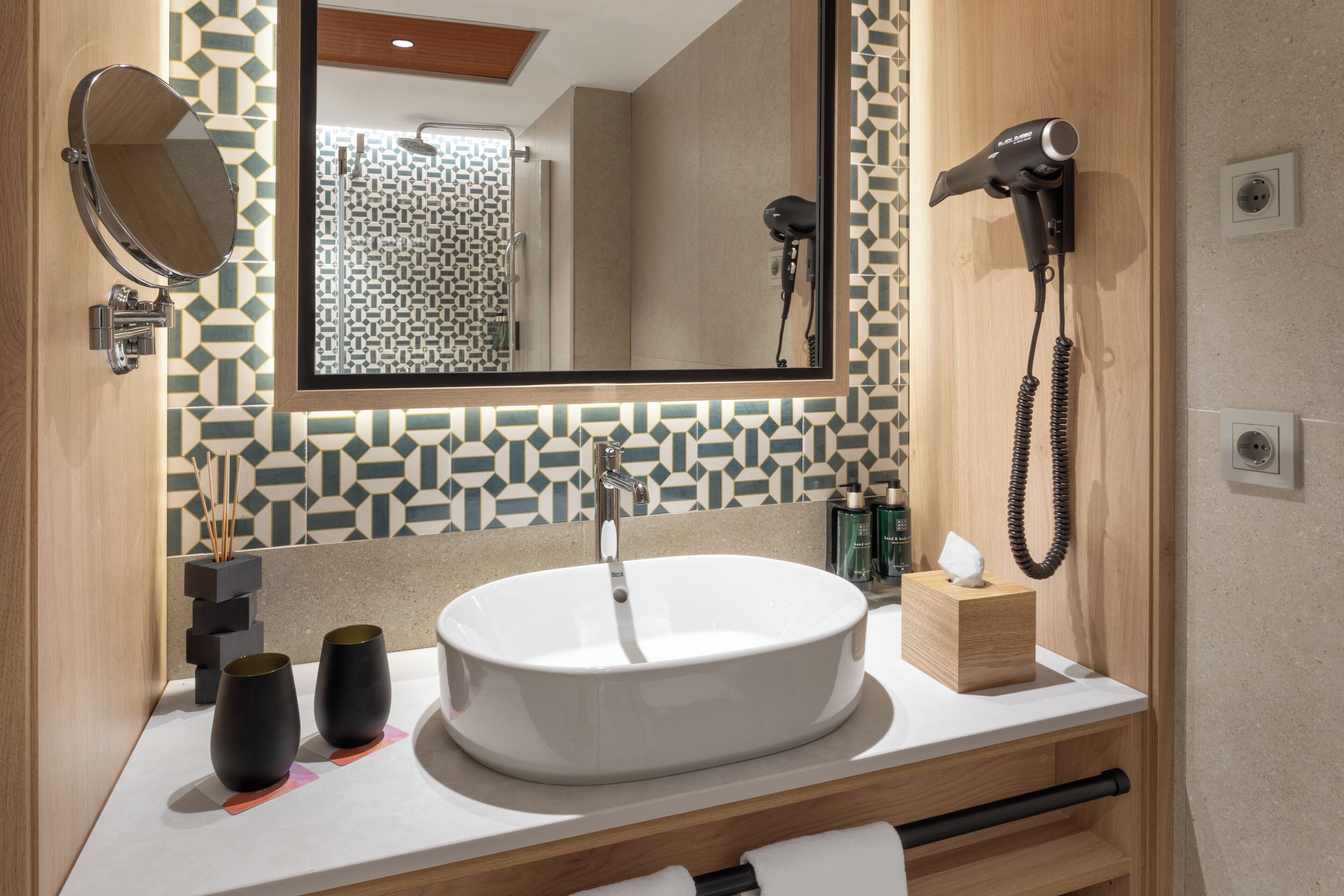 Uma casa de banho moderna com uma pia redonda, um espelho, um secador de cabelo e um porta-toalhas.