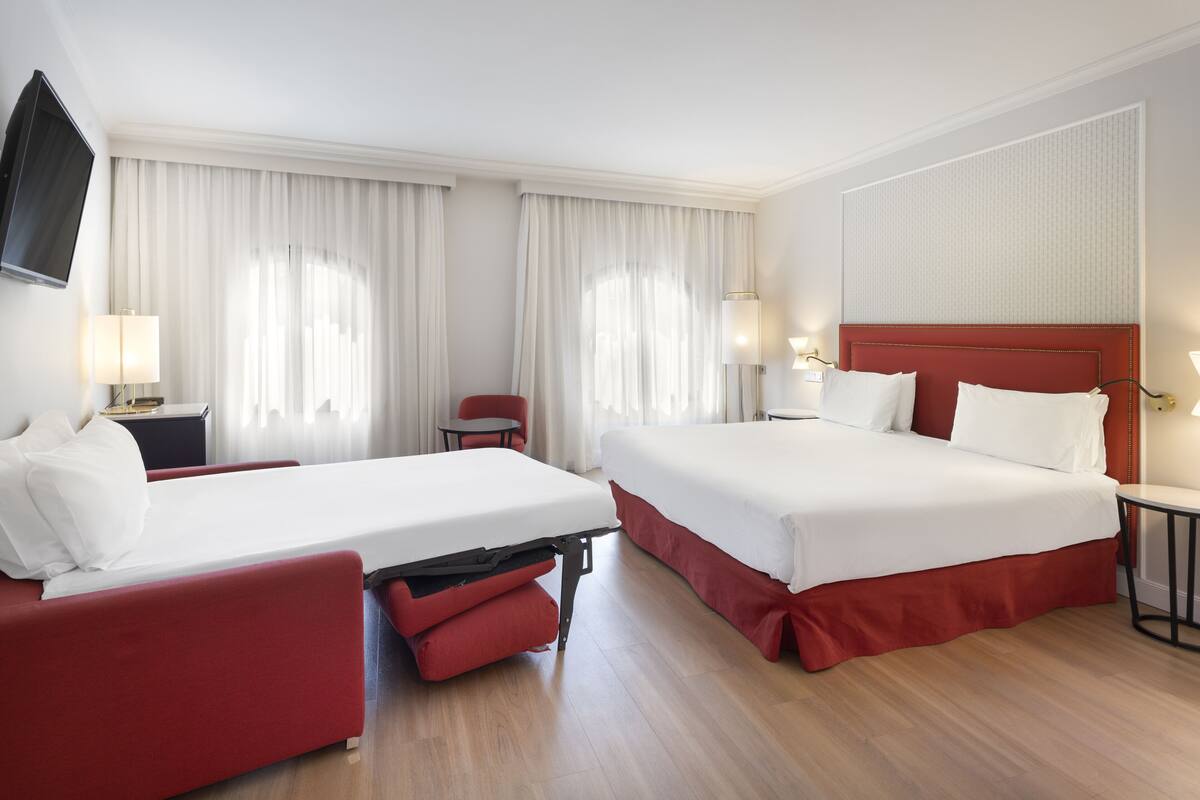 Quarto de hotel com duas camas, uma televisão, uma escrivaninha e uma cadeira.