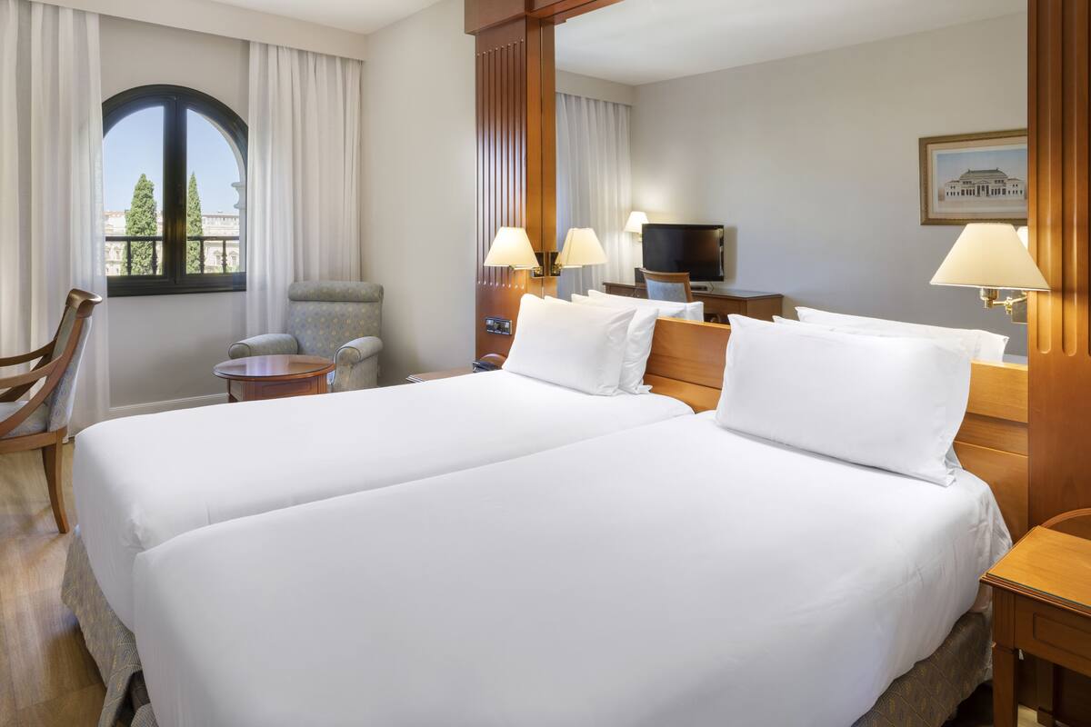 Quarto de hotel com duas camas, televisão, uma cadeira e uma mesa.