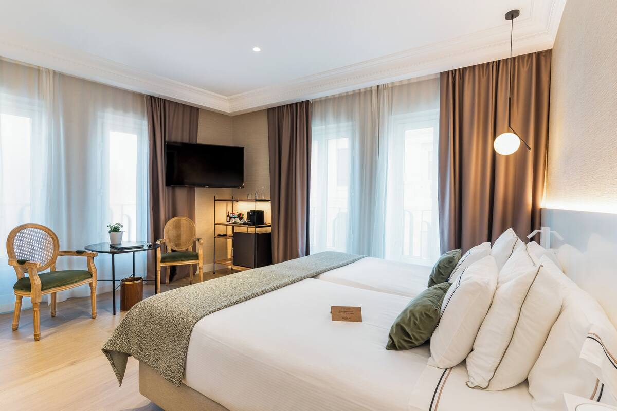 Quarto de hotel com uma cama grande, uma escrivaninha, uma cadeira, uma televisão e cortinas.