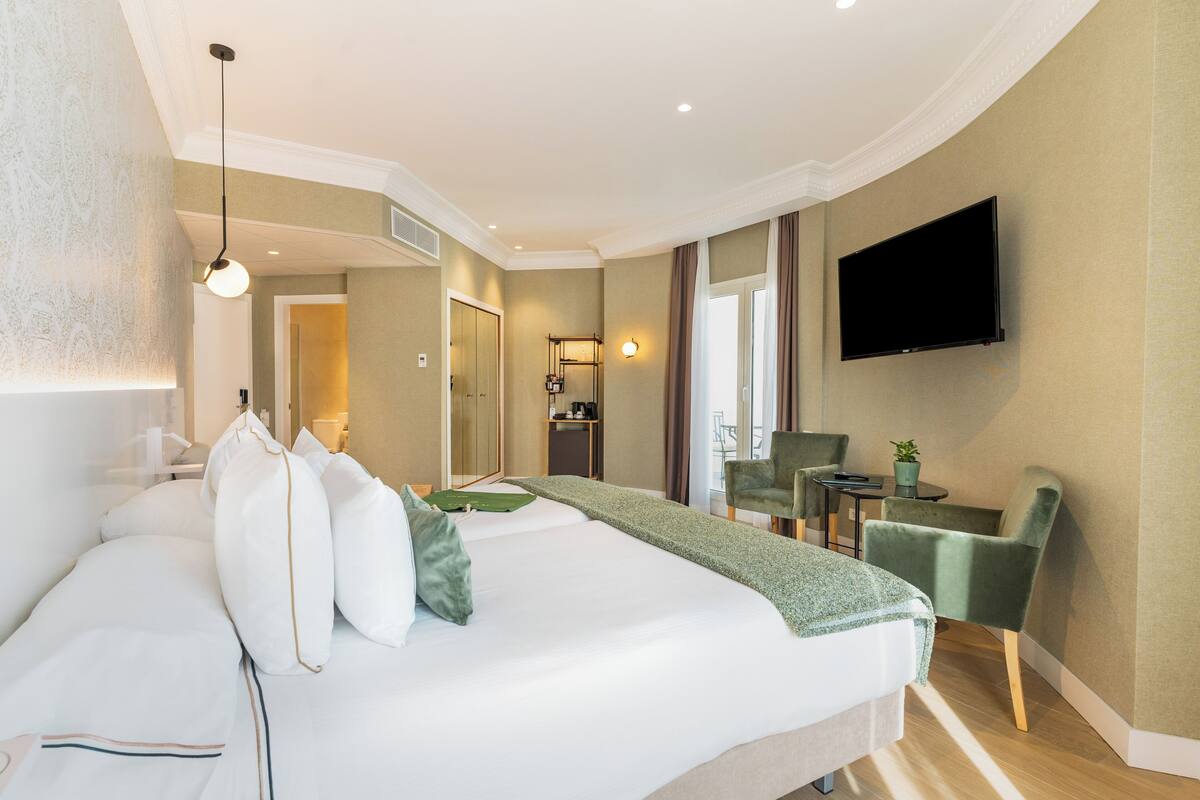 Quarto de hotel com cama, escrivaninha, cadeira, televisão e janela.