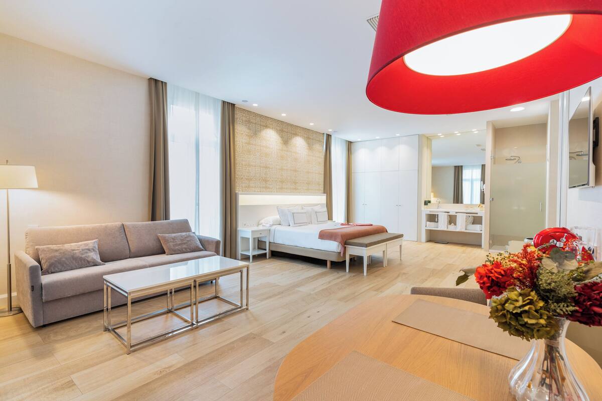 Quarto de hotel moderno com sofá, cama, escrivaninha e uma janela grande.