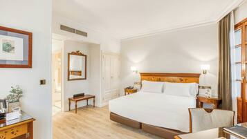 Quarto de hotel com uma cama grande, mesas de cabeceira, escrivaninha, cadeira, espelho e porta.