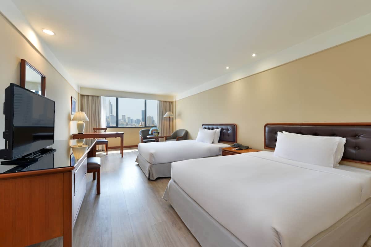 Quarto de hotel com duas camas, uma mesa de trabalho com televisão, uma cadeira e vista para a cidade.