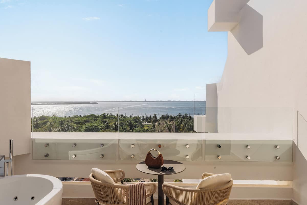 Varanda com vista para o mar, uma banheira, duas cadeiras de vime e uma pequena mesa com uma bolsa e óculos de sol.