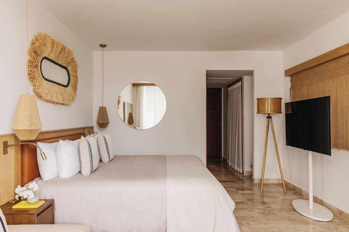 Quarto de hotel com cama, televisão, luminária e espelho.