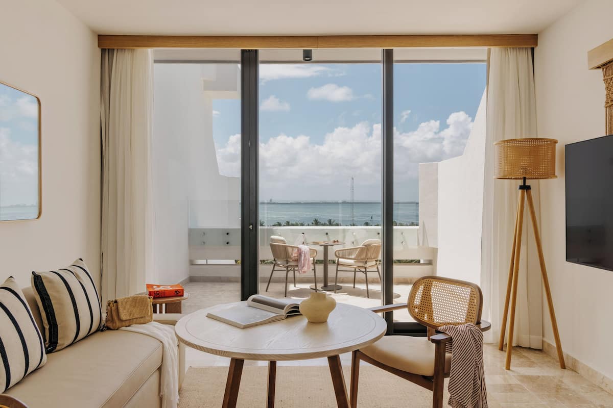 Quarto de hotel moderno com varanda, sofá, mesa redonda e uma cadeira.