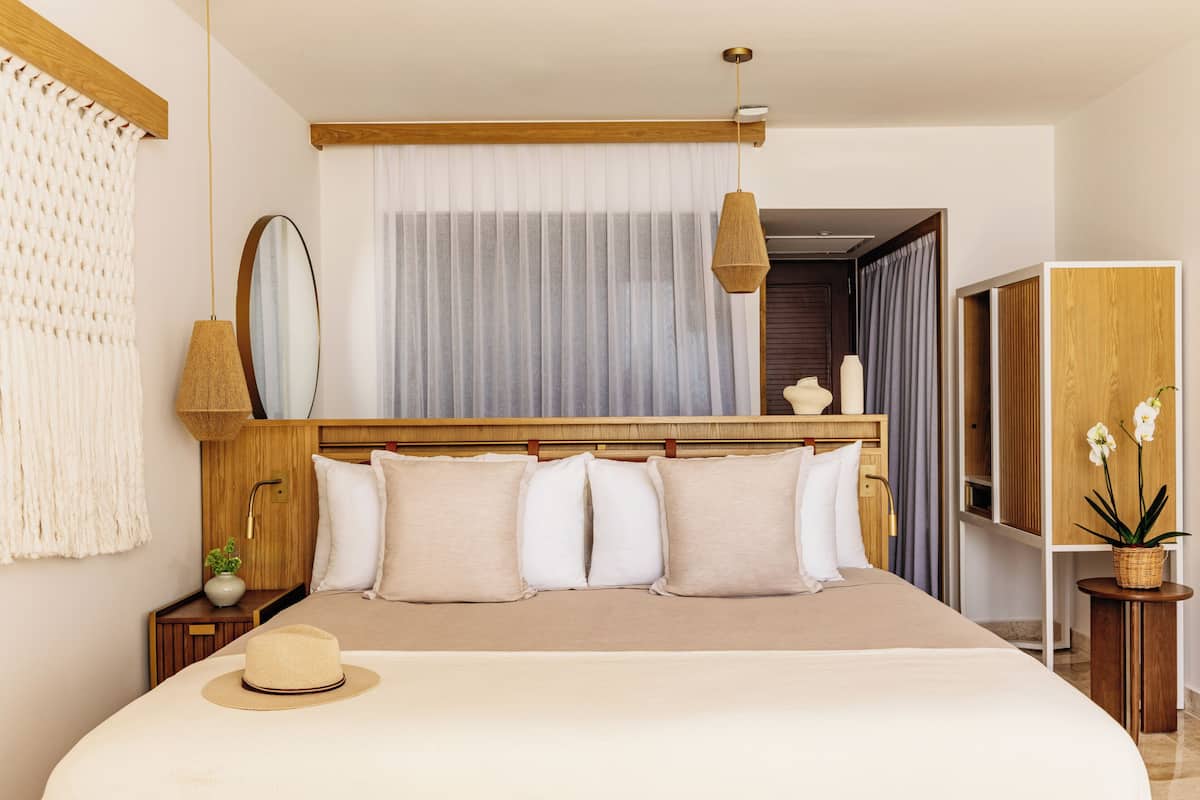 Quarto bem arrumado com cama grande, mesas de cabeceira, espelho e luminária suspensa.