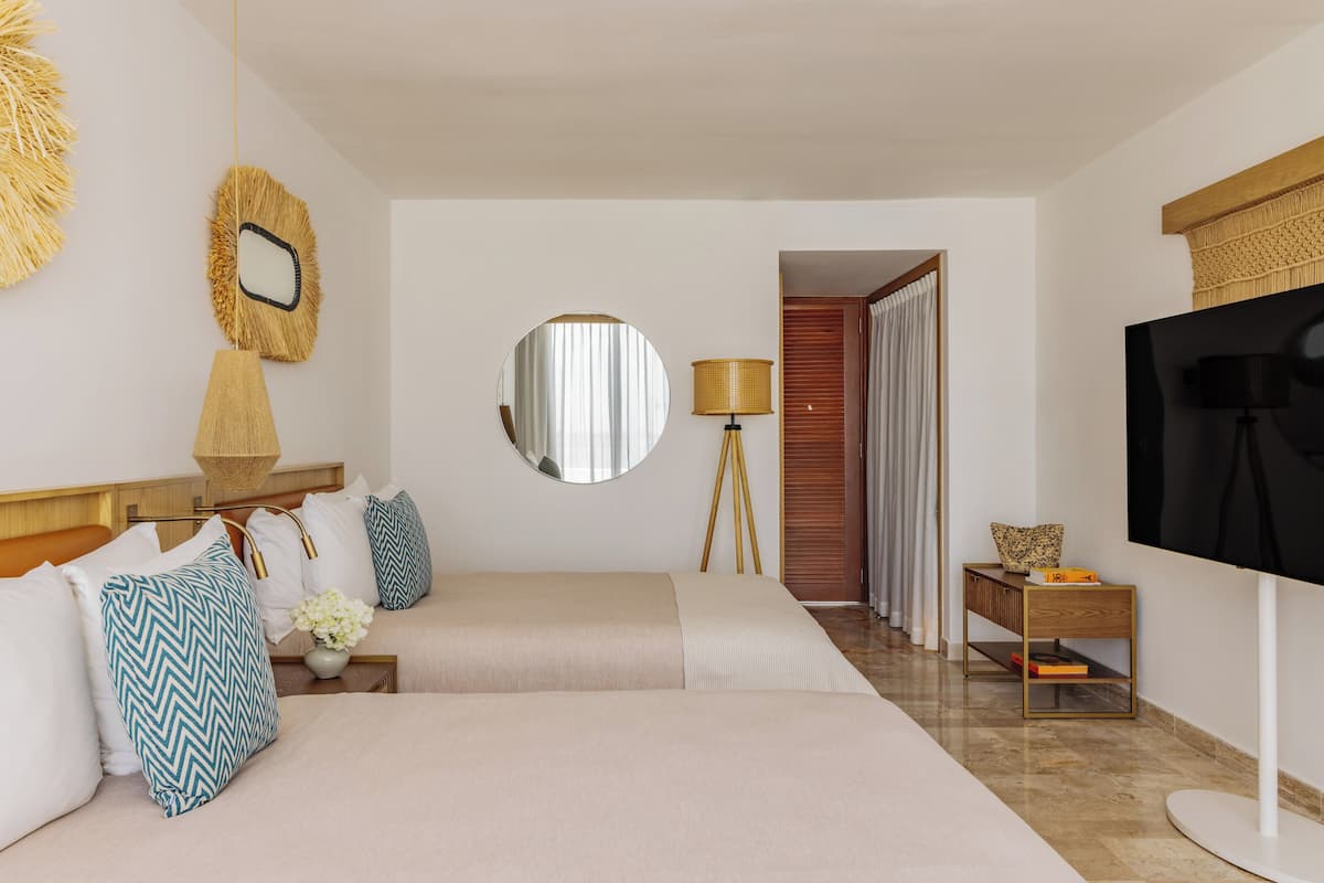 Quarto de hotel com duas camas, uma televisão, um espelho, um abajur e uma mesinha.