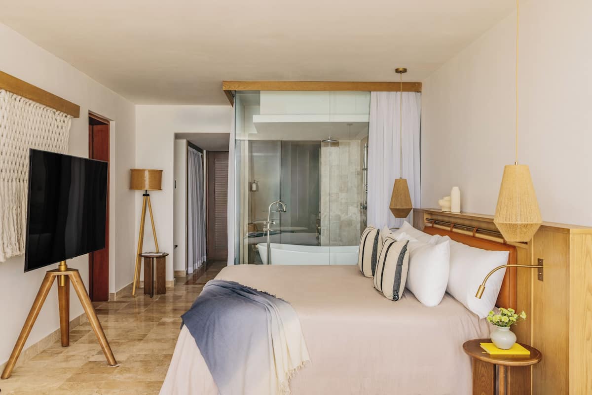 Quarto de hotel com uma cama grande, uma televisão sobre um suporte de tripé, um banheiro com banheira e chuveiro.