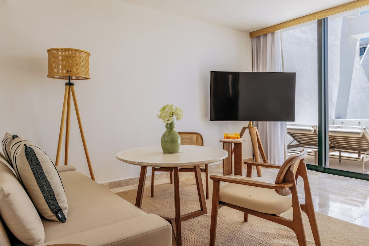 Quarto de hotel moderno com sofá, mesa redonda, televisão e vista para o exterior.