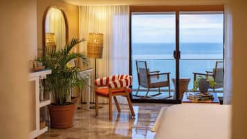Quarto de hotel com cama, uma cadeira, uma mesa, um vaso de plantas e vista para o mar.