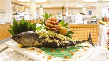 Prato de frutos do mar com peixe inteiro, camarão e abacaxi sobre um suporte branco.