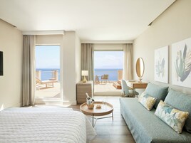 Quarto de hotel com cama, sofá, escrivaninha e varanda com vista para o mar.