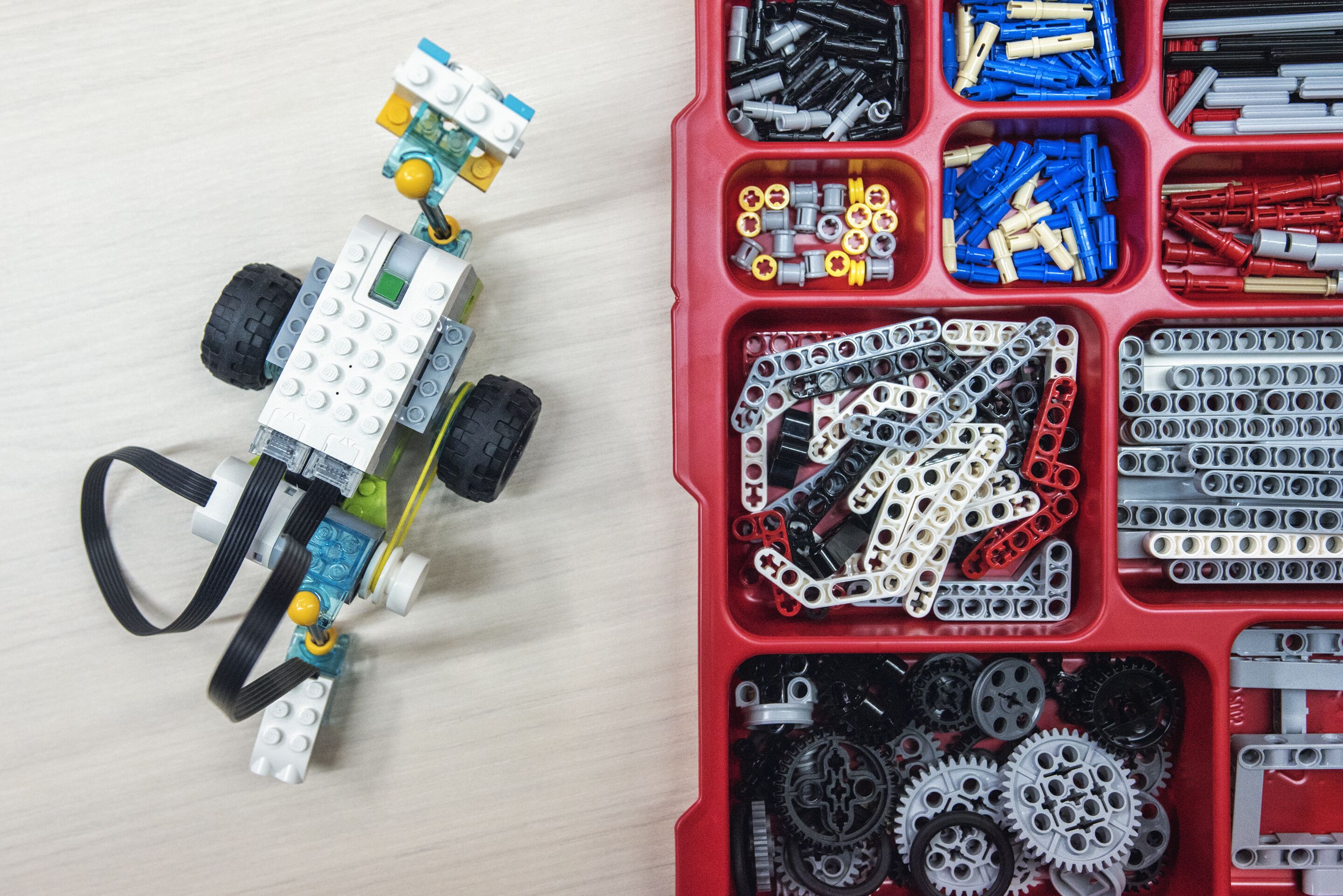 Um robô LEGO Technic sobre uma superfície de madeira clara, ao lado de uma caixa de ferramentas vermelha com várias peças mecânicas.