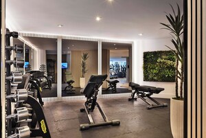 Uma academia com equipamentos de ginástica, um espelho e uma parede verde com plantas.