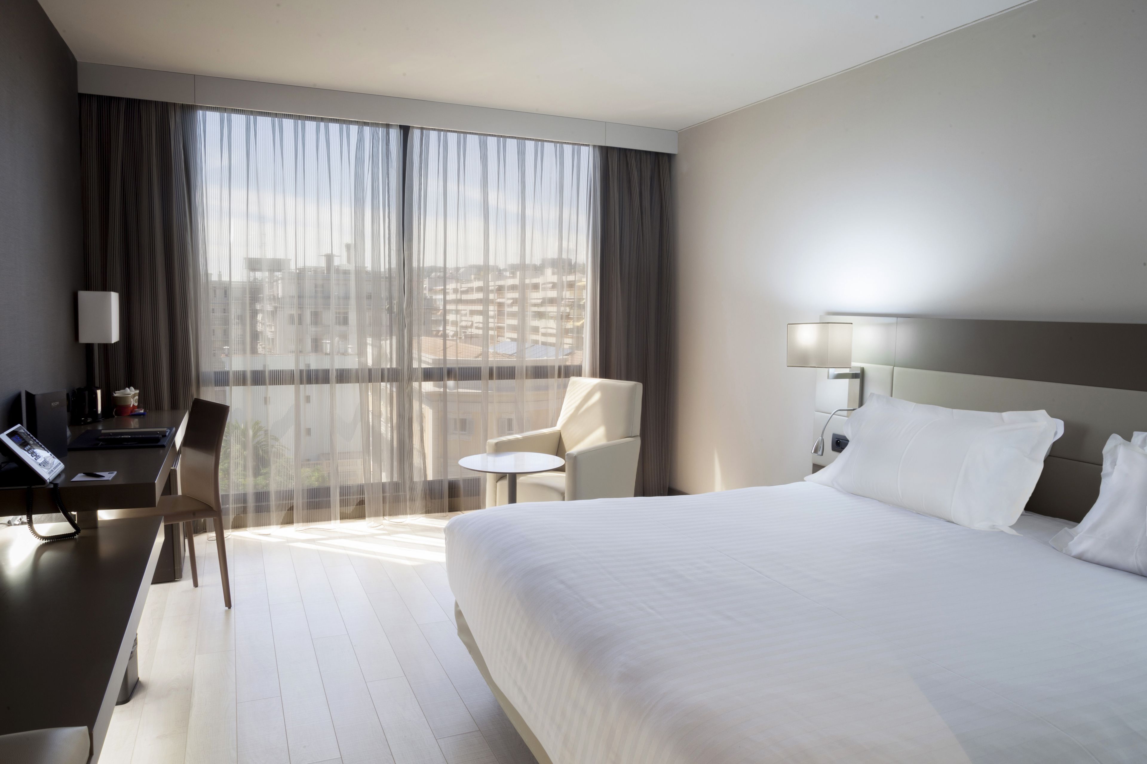 Quarto de hotel com uma cama grande, uma escrivaninha com computador, uma cadeira e uma mesinha.
