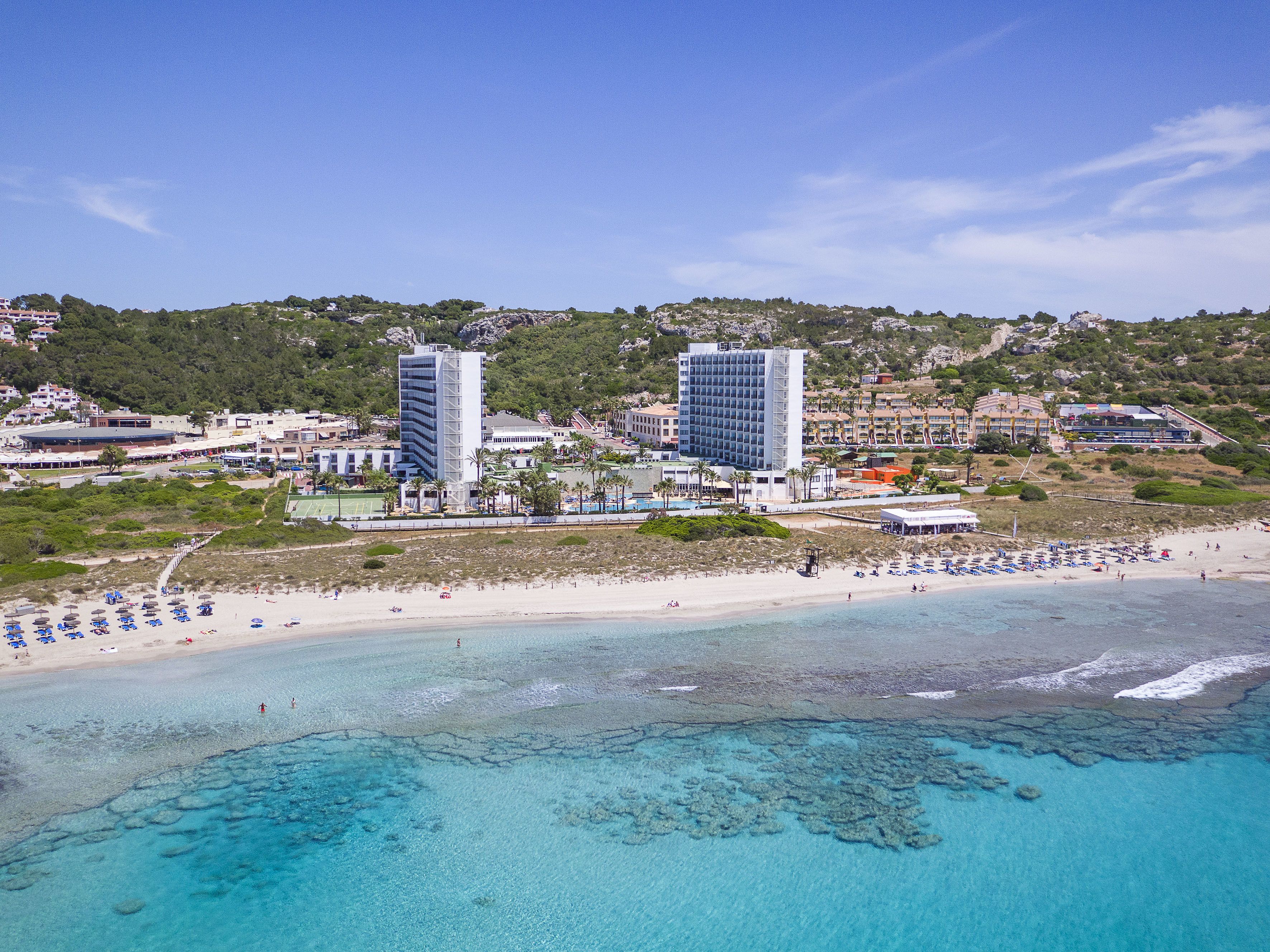 Um hotel à beira-mar com vários edifícios altos, uma praia arenosa e águas azul-claras.