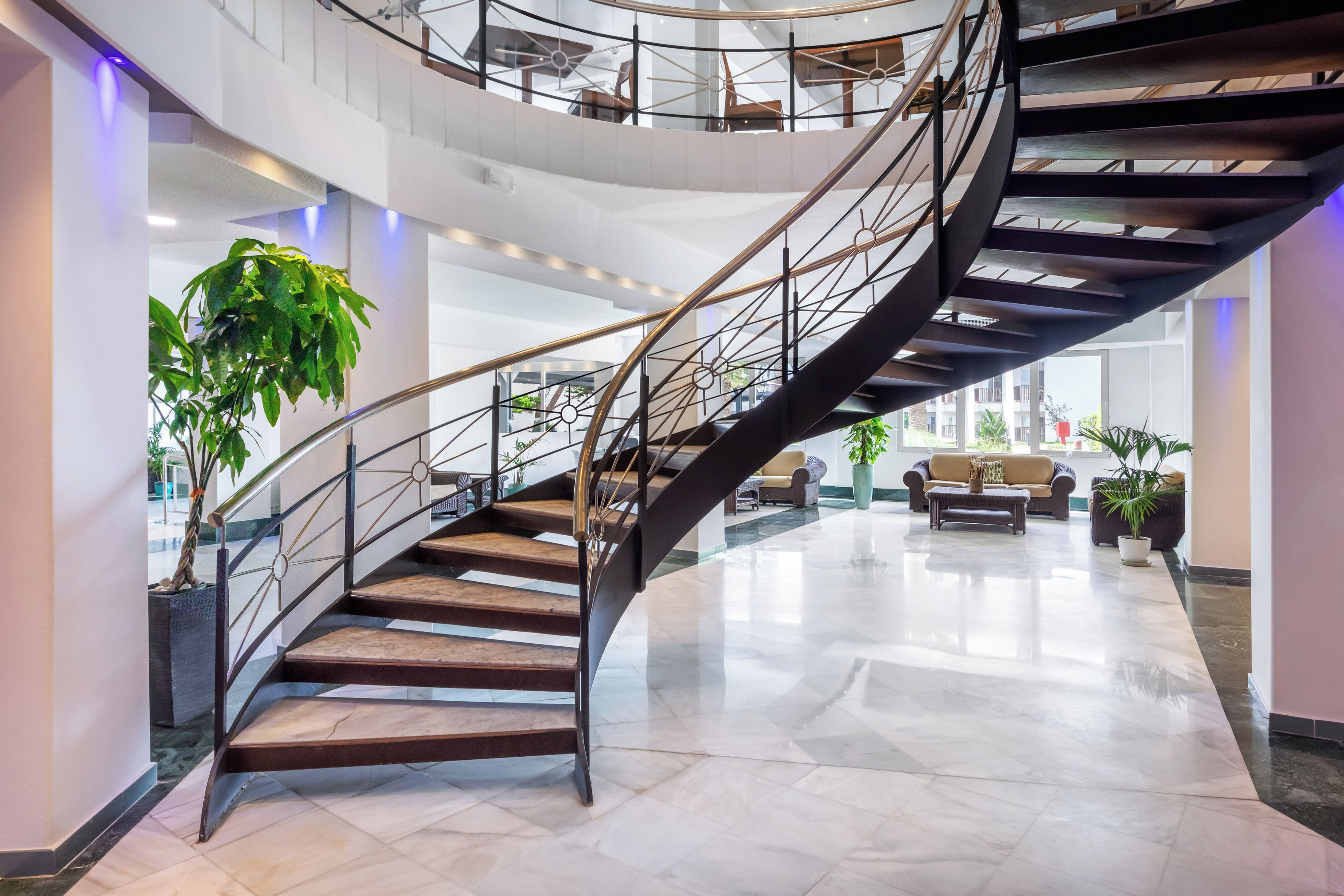 Um interior moderno com escada em espiral, piso de mármore e plantas dentro de casa.