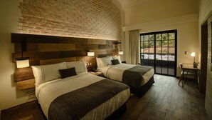 Quarto de hotel com duas camas, parede de destaque em tijolo, cabeceira de madeira e vista através de uma grande janela.