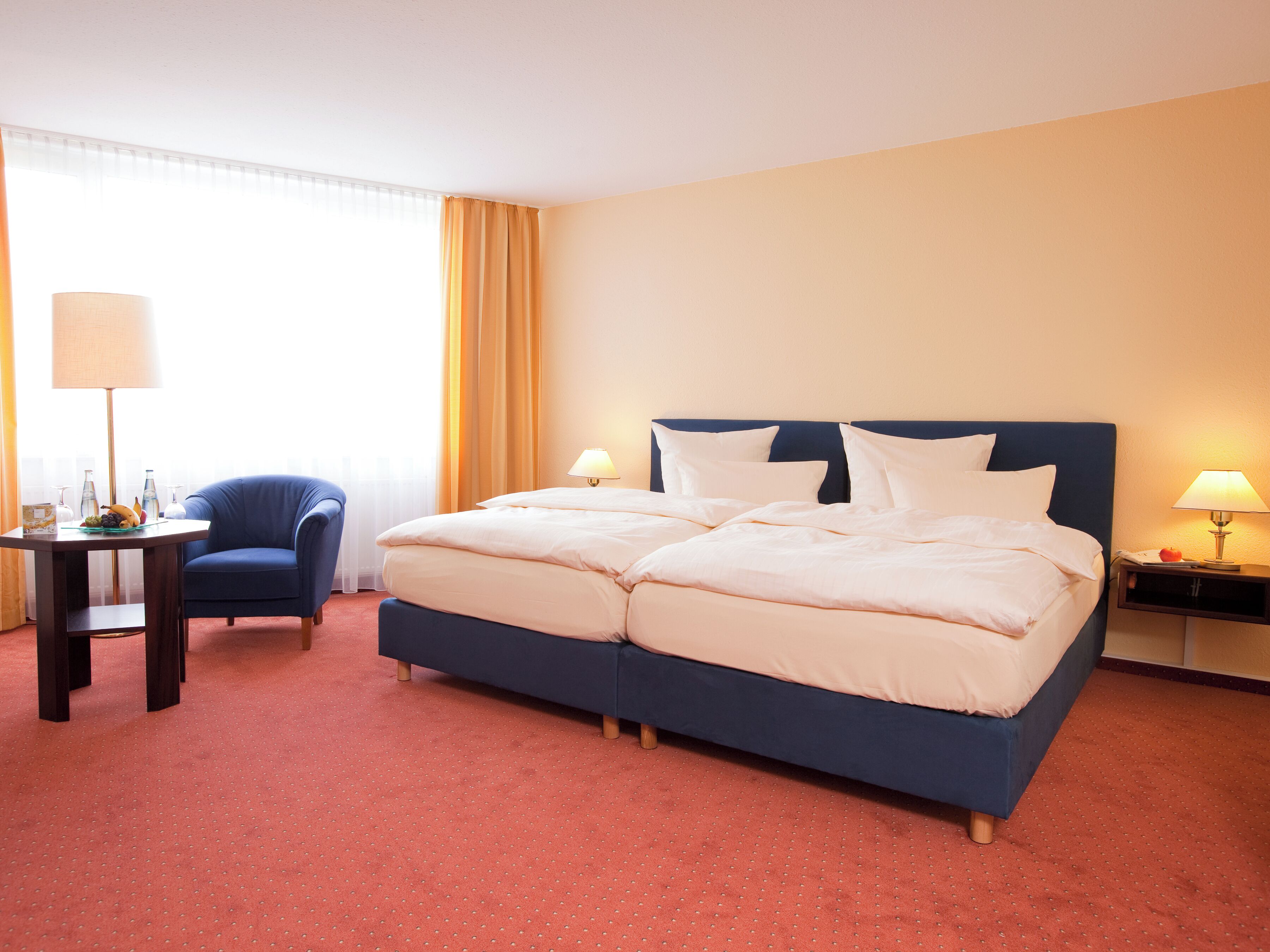 Quarto de hotel com uma cama grande, uma cadeira, uma mesa com abajur e uma mesa de cabeceira com abajur.
