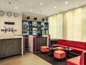 Uma área de recepção com bar, assentos e relógios nas paredes.