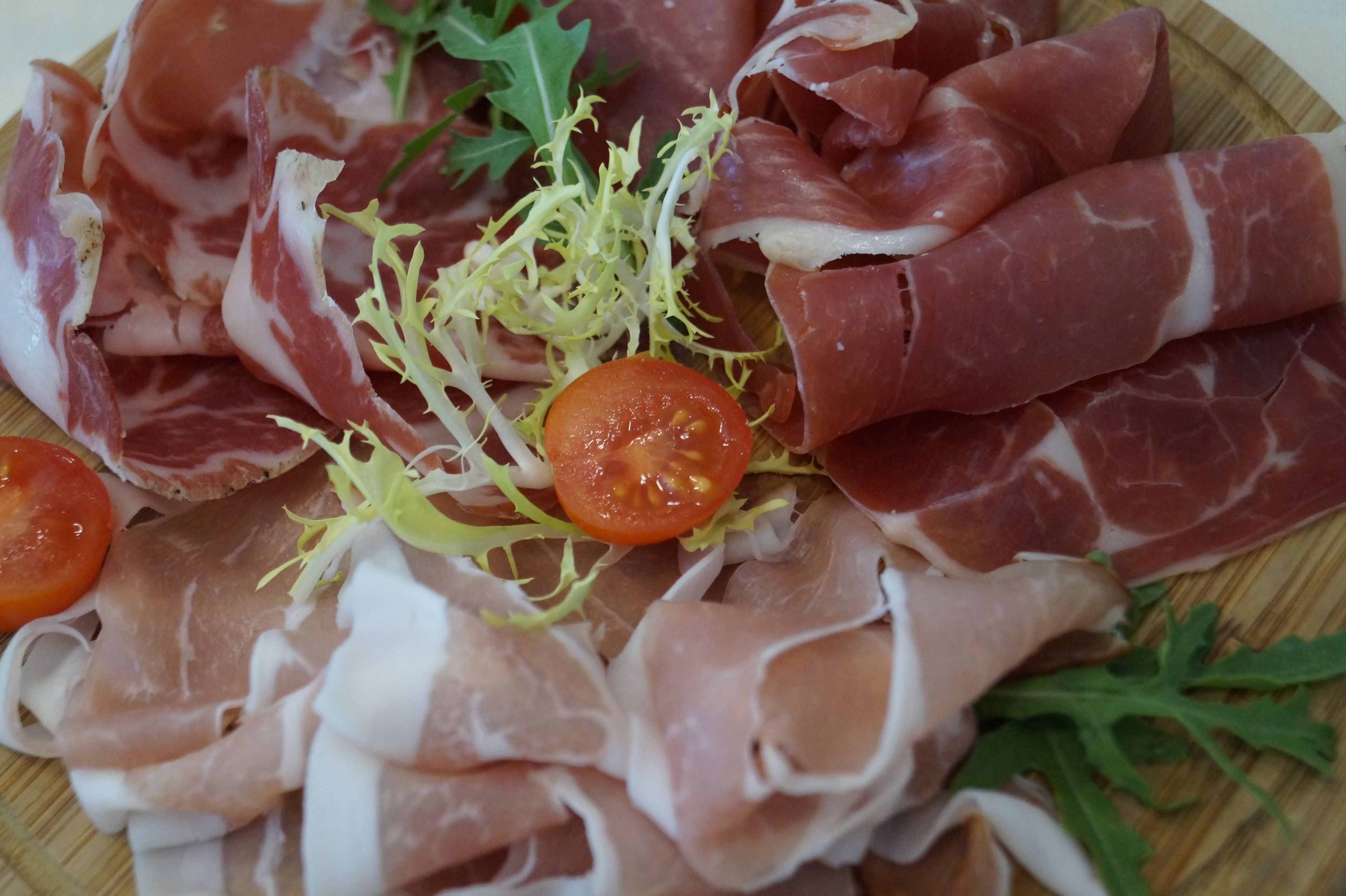 Tábua de madeira com presunto cru fatiado, tomates cereja e rúcula.