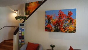 Um hall com escada, dois poltronas com almofadas vermelhas, uma mesa pequena com um vaso e um quadro de flores na parede.