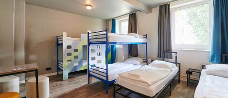 Um quarto de dormitório com beliches, uma escrivaninha e uma janela com cortinas.