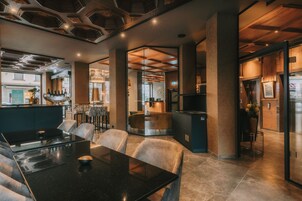 Interior moderno de restaurante com mesa preta, cadeiras acolchoadas, área de bar e um relógio à vista.