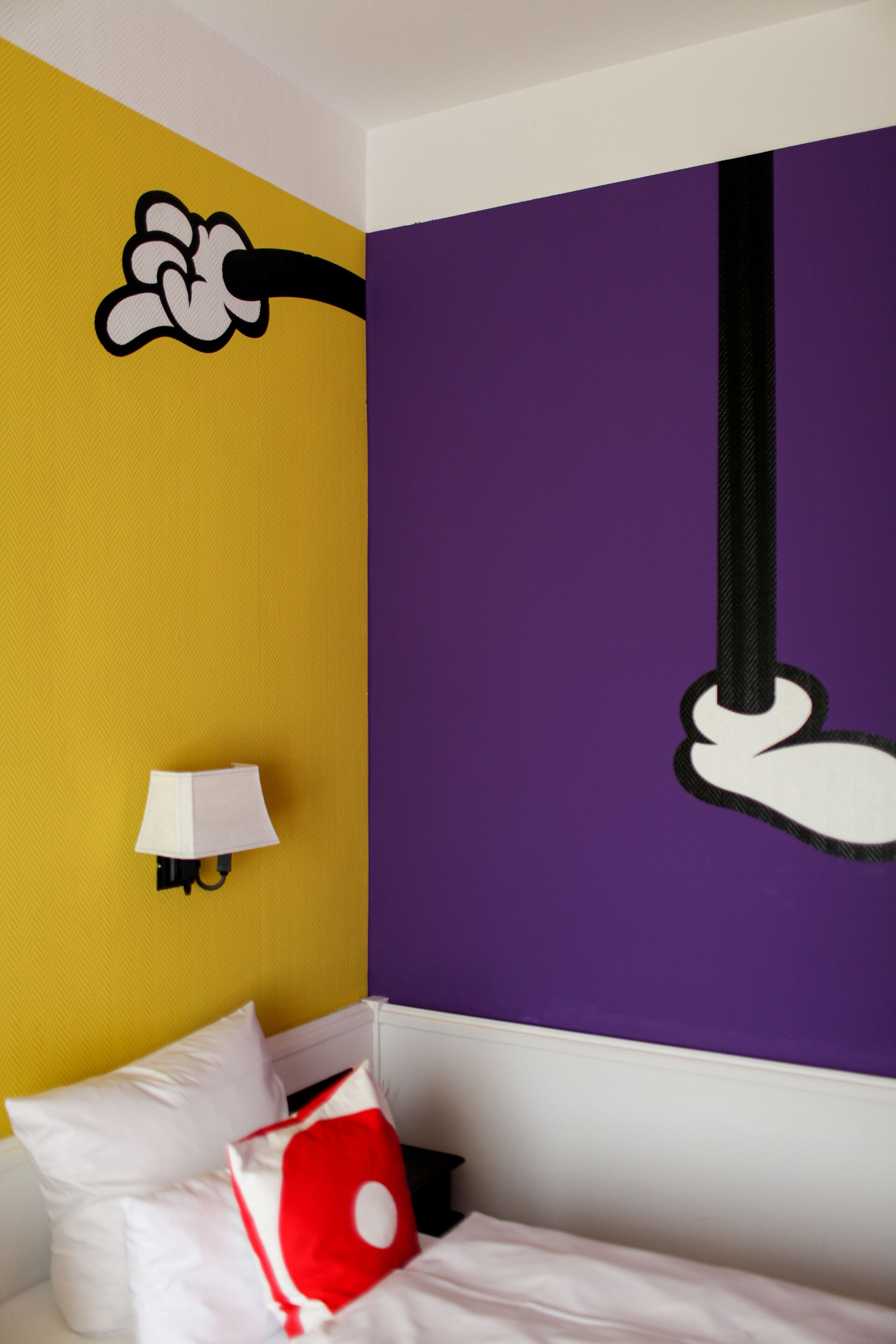 Quarto com cama, luminária na parede e um mural grande.