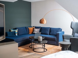 Uma sala de estar moderna com um sofá azul, um laptop em uma mesinha e um abajur diferente.