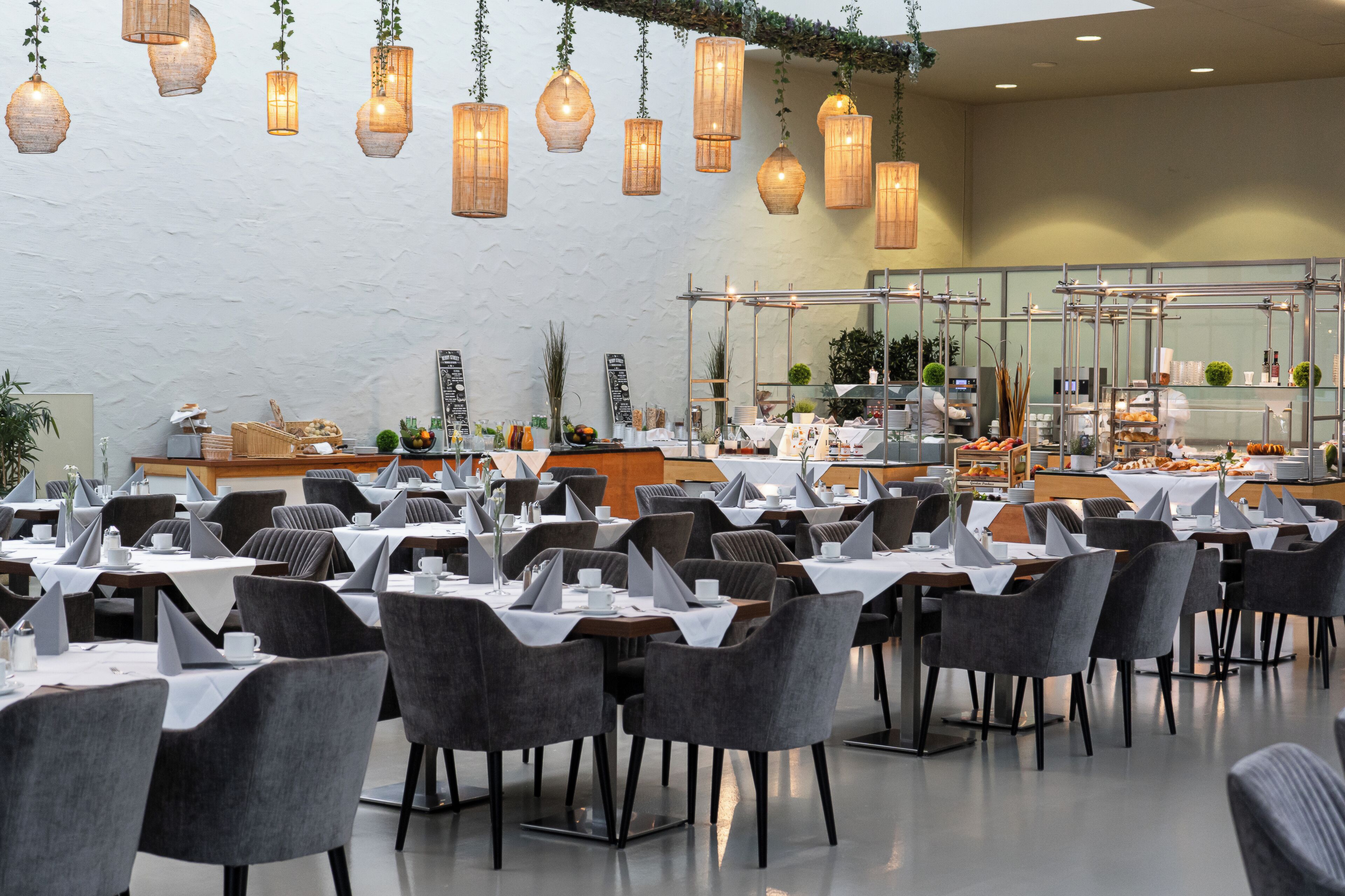 Uma ampla área de jantar com várias mesas e cadeiras, espaço para buffet e luminárias pendentes estilo lanterna.