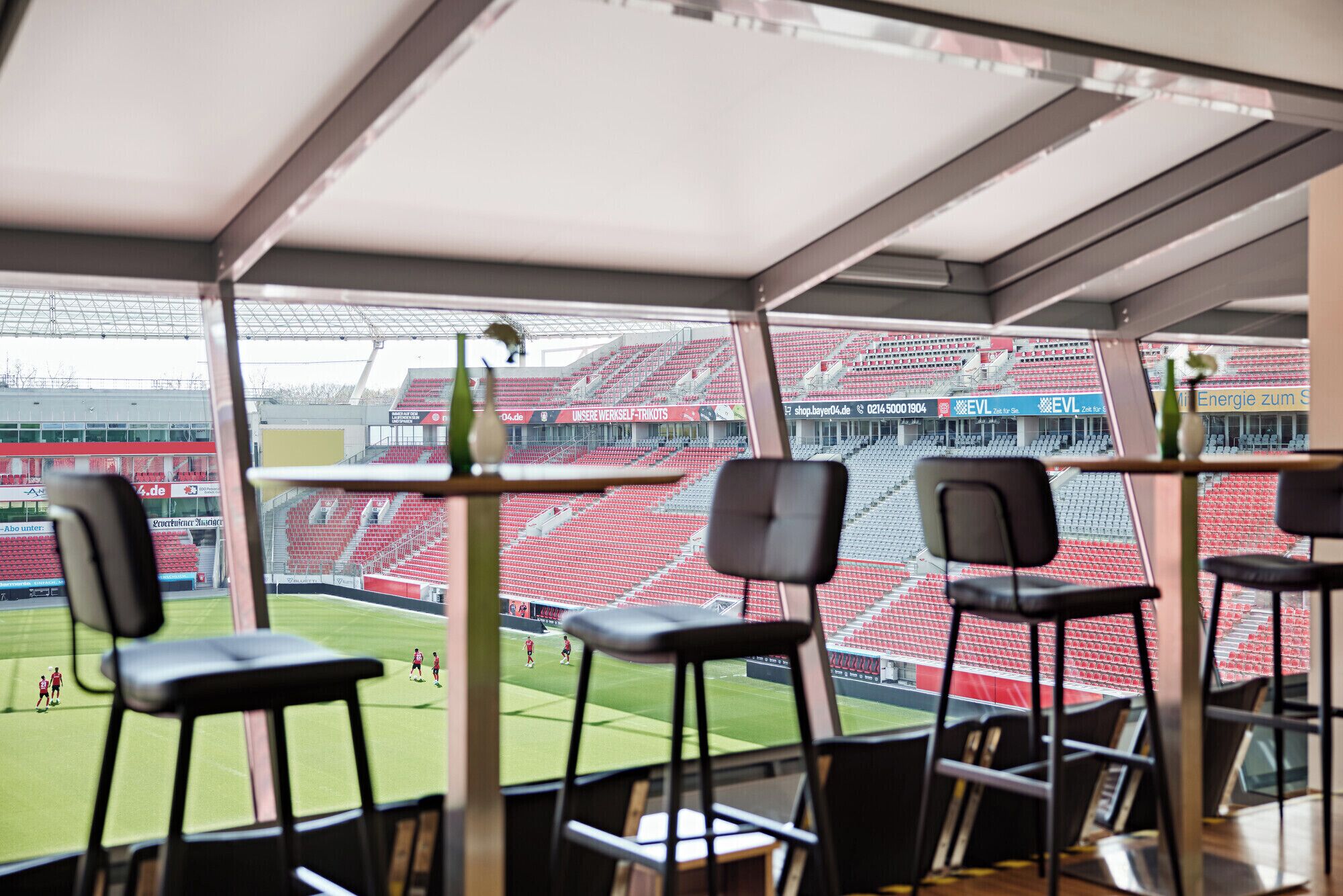 Vista de estádio vista de dentro de um prédio, com assentos vermelhos vazios e algumas cadeiras pretas em primeiro plano.