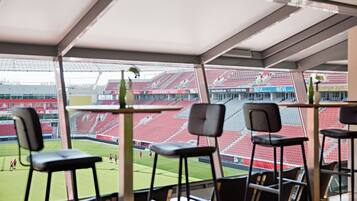 Vista de estádio vista de dentro de um prédio, com assentos vermelhos vazios e algumas cadeiras pretas em primeiro plano.