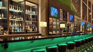 Uma área de bar com vários bancos, prateleiras cheias de garrafas de bebidas e grandes telas exibindo conteúdo.