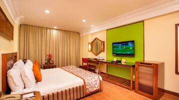 Quarto de hotel com cama, escrivaninha, televisão e espelho.