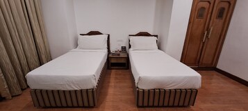 Quarto com duas camas de solteiro, cabeceiras de madeira, mesa de cabeceira com abajur e armário de madeira.
