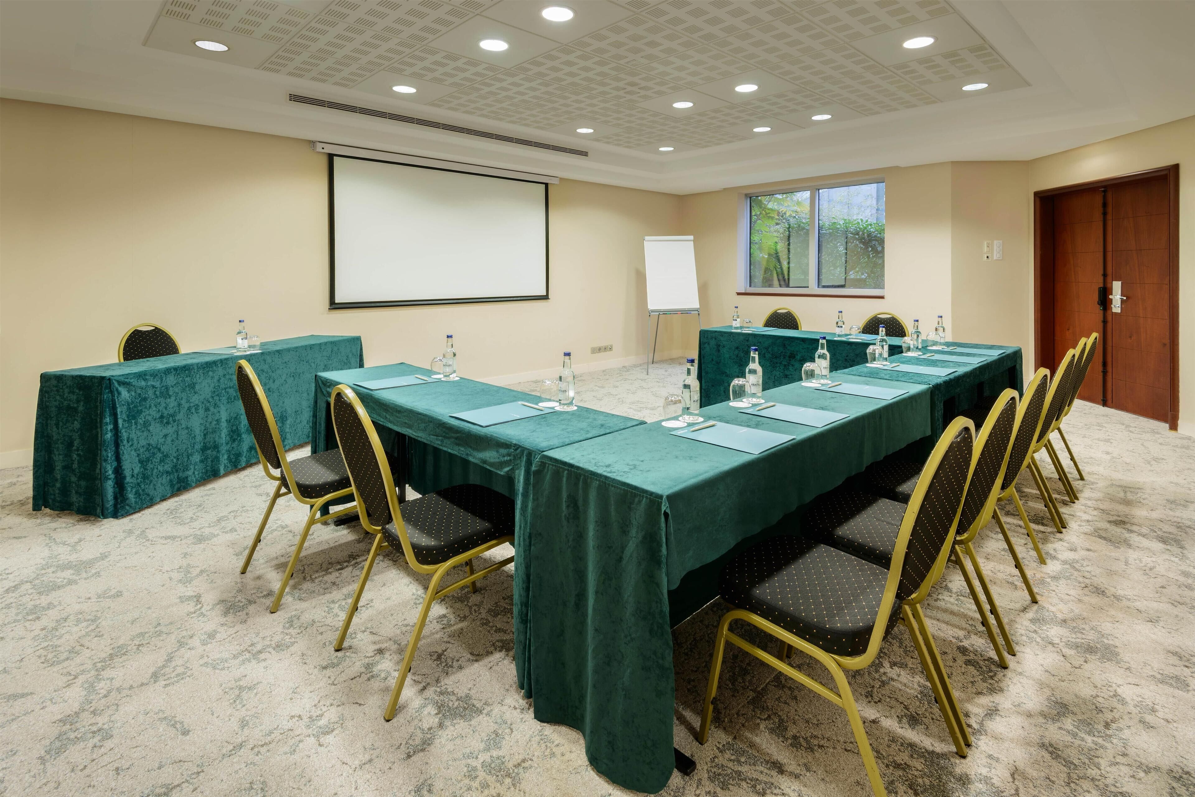 Uma sala de conferência com uma mesa comprida, cadeiras, uma tela de projetor e um quadro branco.