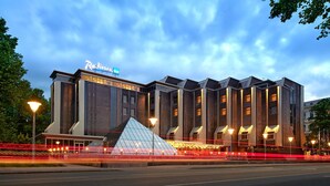 Um hotel moderno com uma imponente entrada em forma de pirâmide de vidro, uma placa com a inscrição 'Radisson' e uma série de janelas verticais.