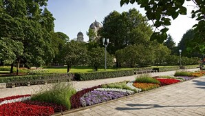 Um jardim ajardinado com um caminho pavimentado, bancos e diversos canteiros de flores.