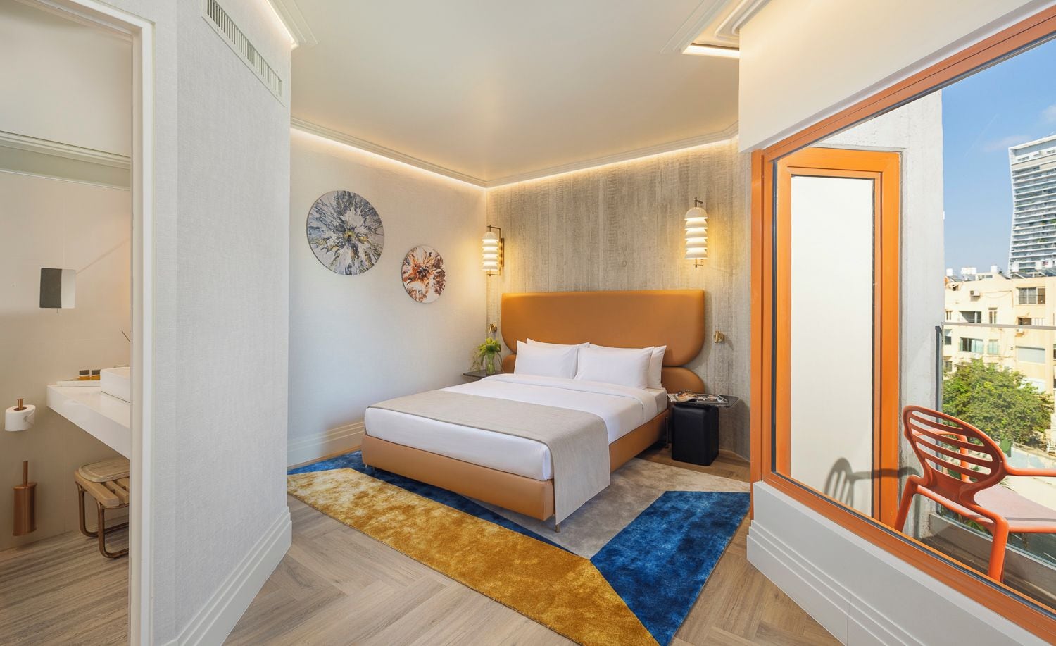 Quarto de hotel moderno com uma cama grande, banheiro e varanda com vista para a cidade.
