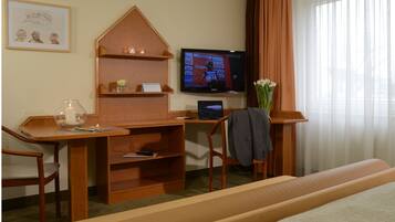 Quarto de hotel com uma escrivaninha de madeira, um laptop, uma televisão, uma cama e uma cadeira.