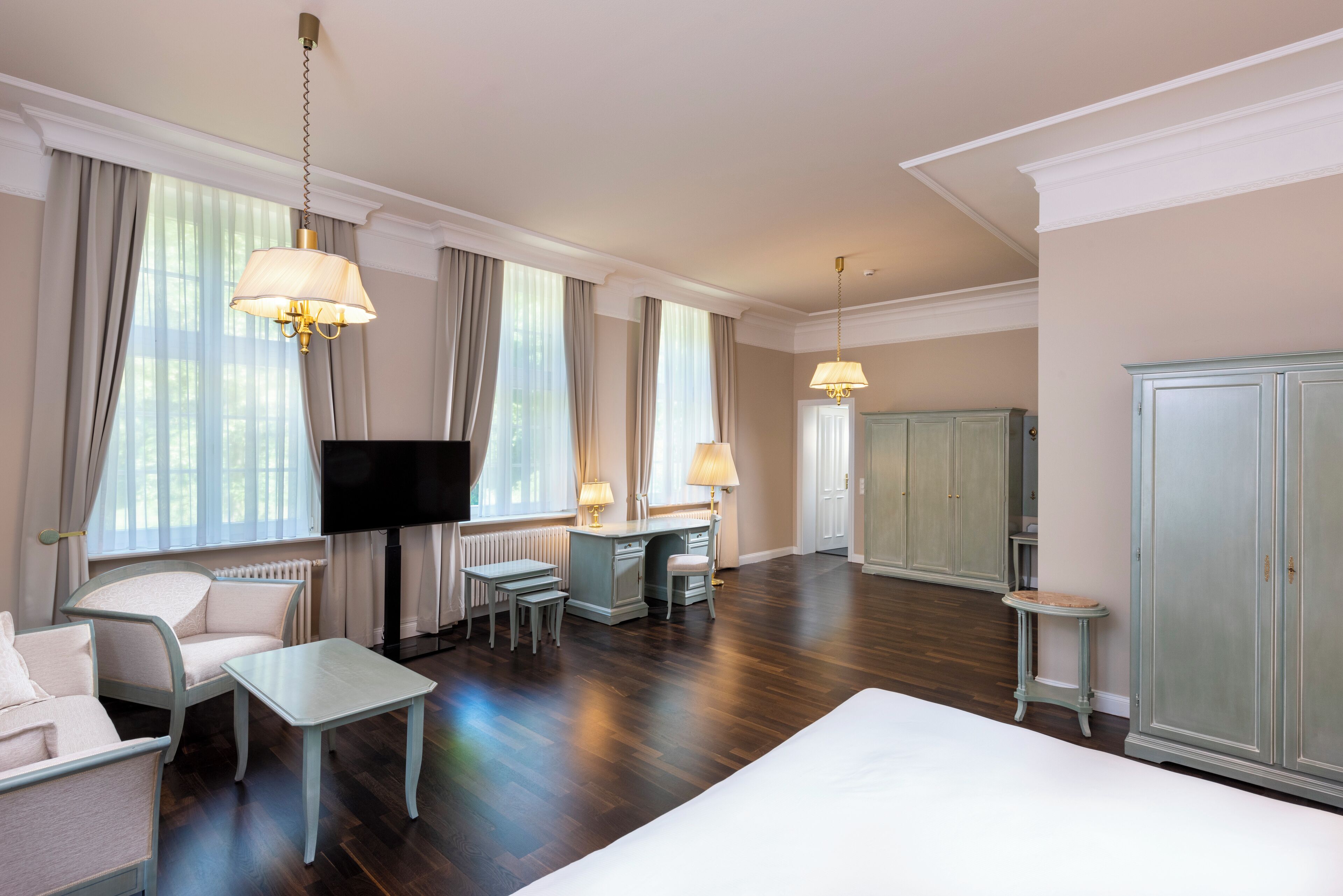 Quarto de hotel com uma cama, uma escrivaninha, uma cadeira, uma televisão e um guarda-roupa.