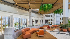 Um hall amplo com design moderno, com uma grande área de estar com sofás laranja e piso de mármore.