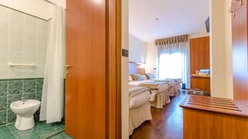 Quarto de hotel com chuveiro, vaso sanitário e duas camas.