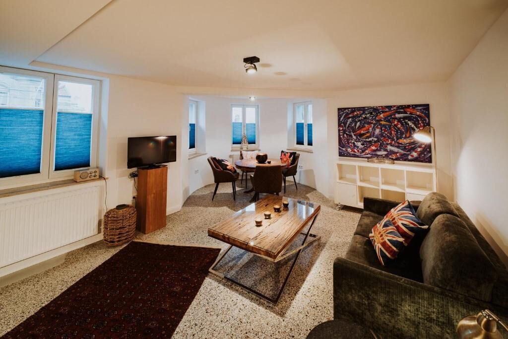 Uma sala de estar moderna com área de jantar, janelas amplas, TV de tela plana e um quadro abstrato colorido.
