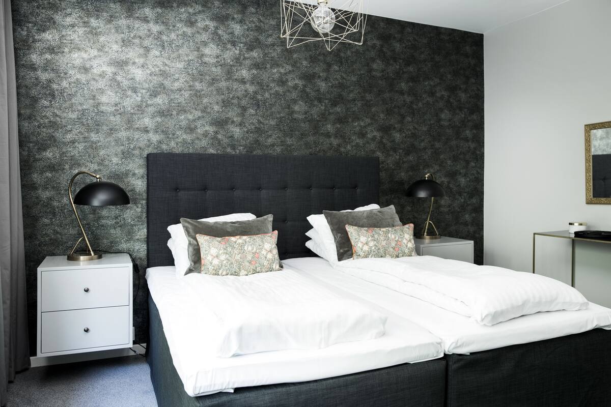 Um quarto moderno com uma cama grande, duas mesas de cabeceira e uma parede escura com textura.