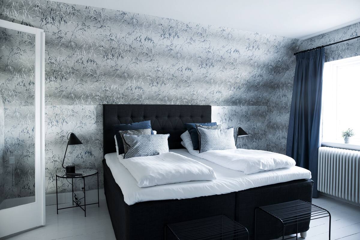 Quarto moderno com uma cama grande, uma mesa de cabeceira e vista para o exterior.